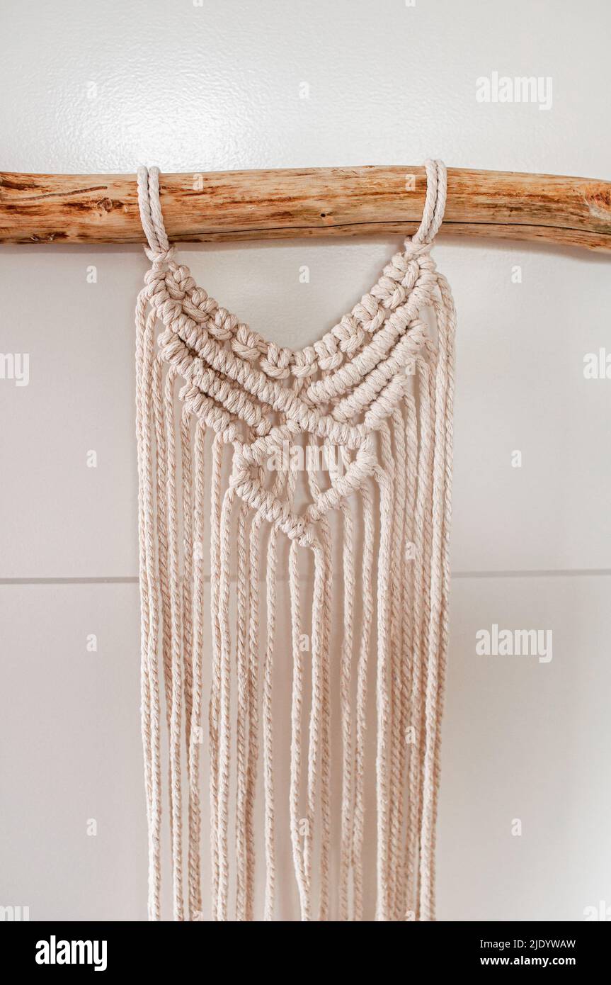 Wall decor in the style of weaving macrame handmade from beige natural threads on a white ...