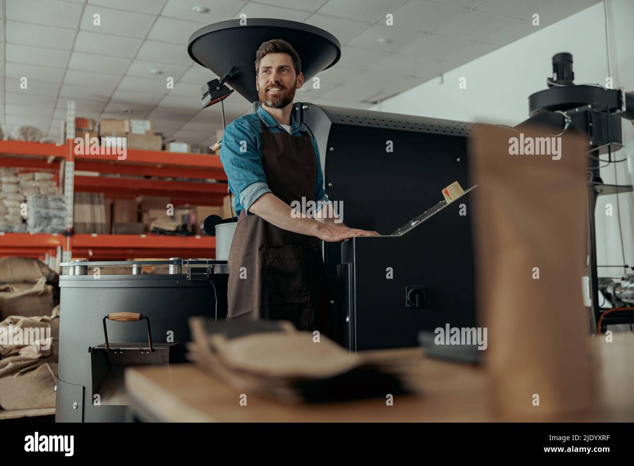 Smiling Business owner operating a modern coffee bean roasting machine ...
