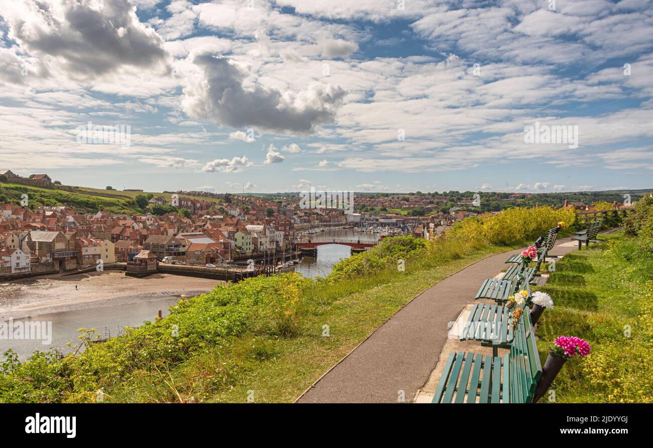 A line of benches overlook a harbur and a beach. A marina is in the ...