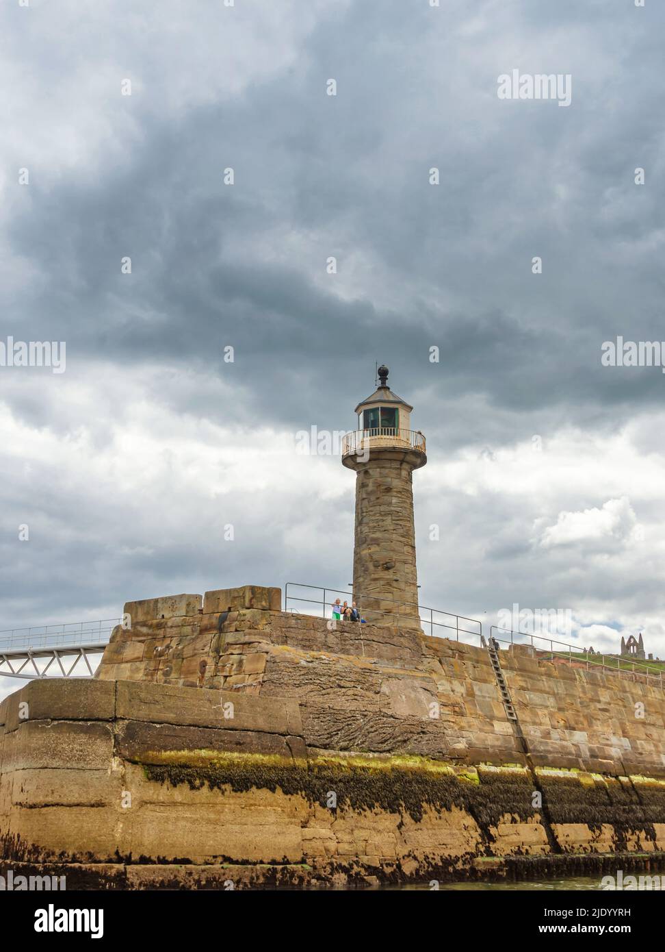 Low angled view of a lighthouse and pier. People are near some railings ...