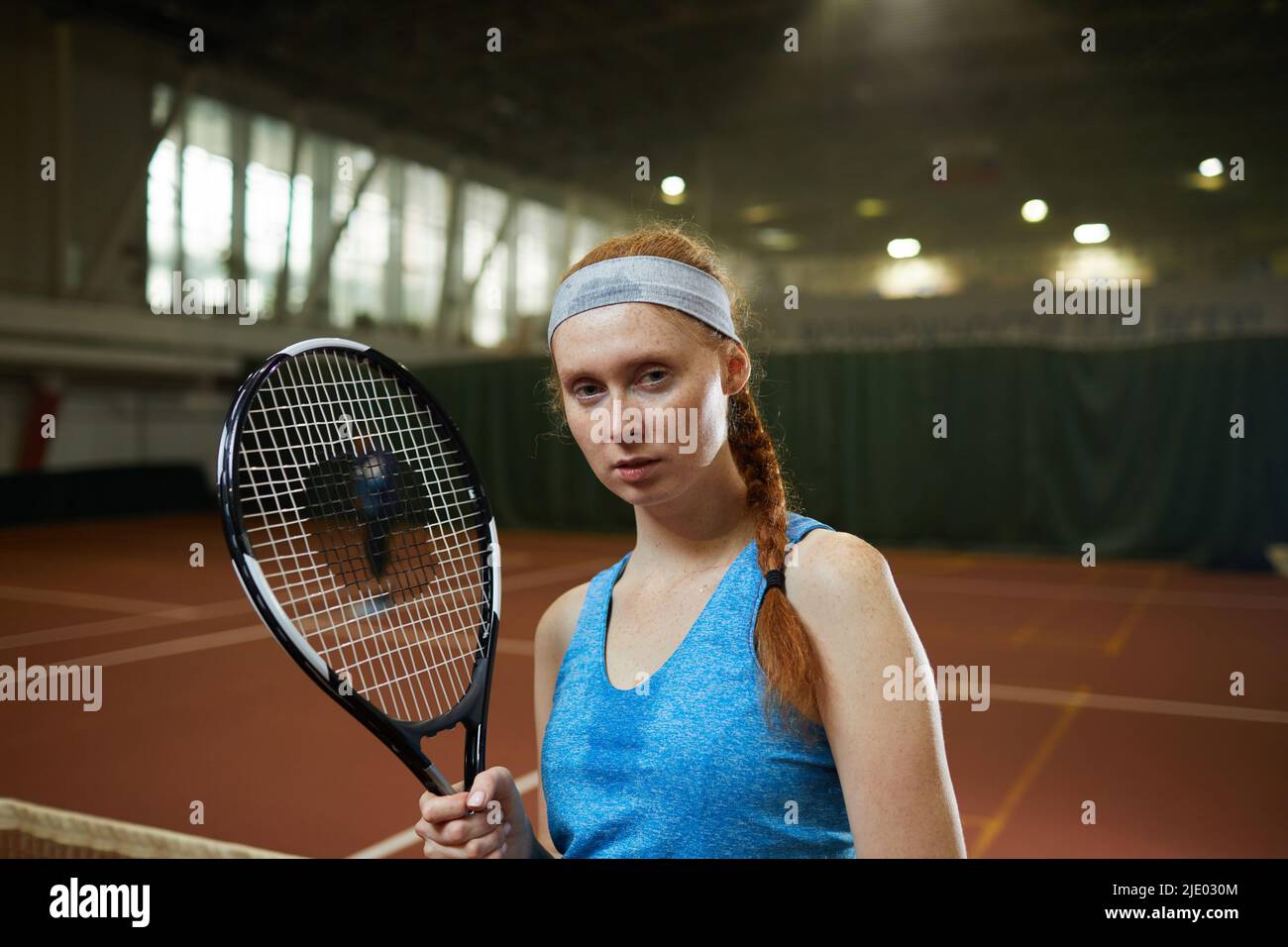 Portrait of serious sweaty young redhead woman in sports headband ...