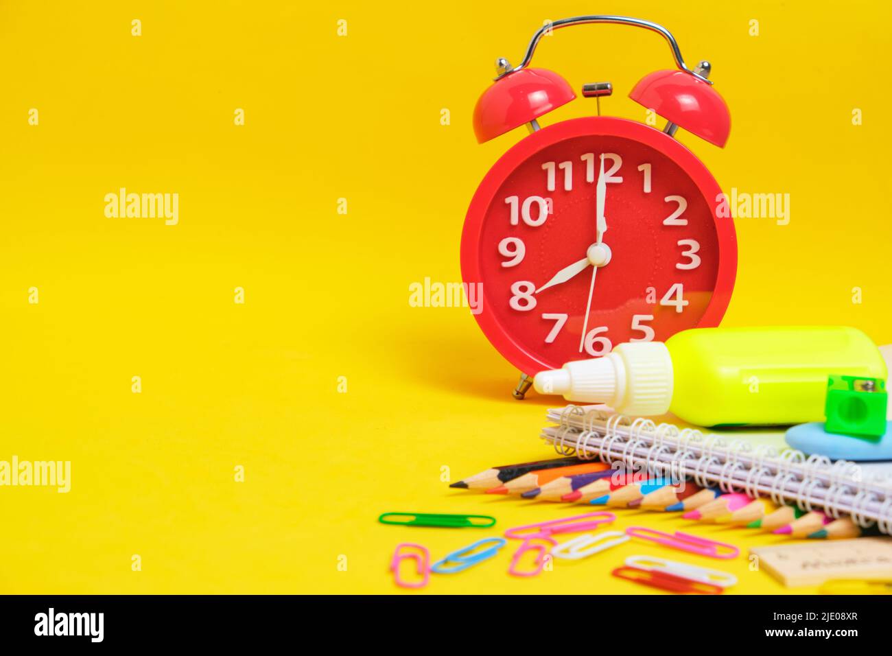 Red alarm clock and school supplies yellow background.Preparing child ...