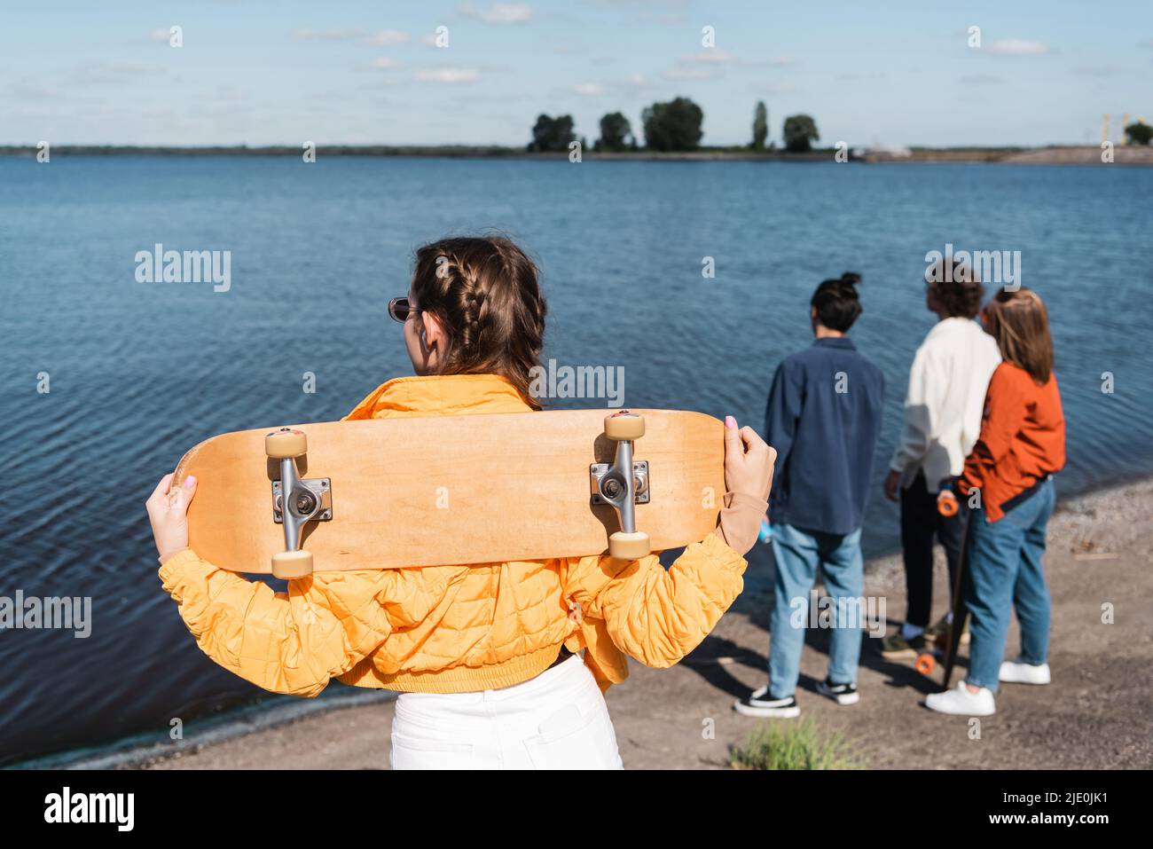 back view of young woman with skateboard standing near river and ...
