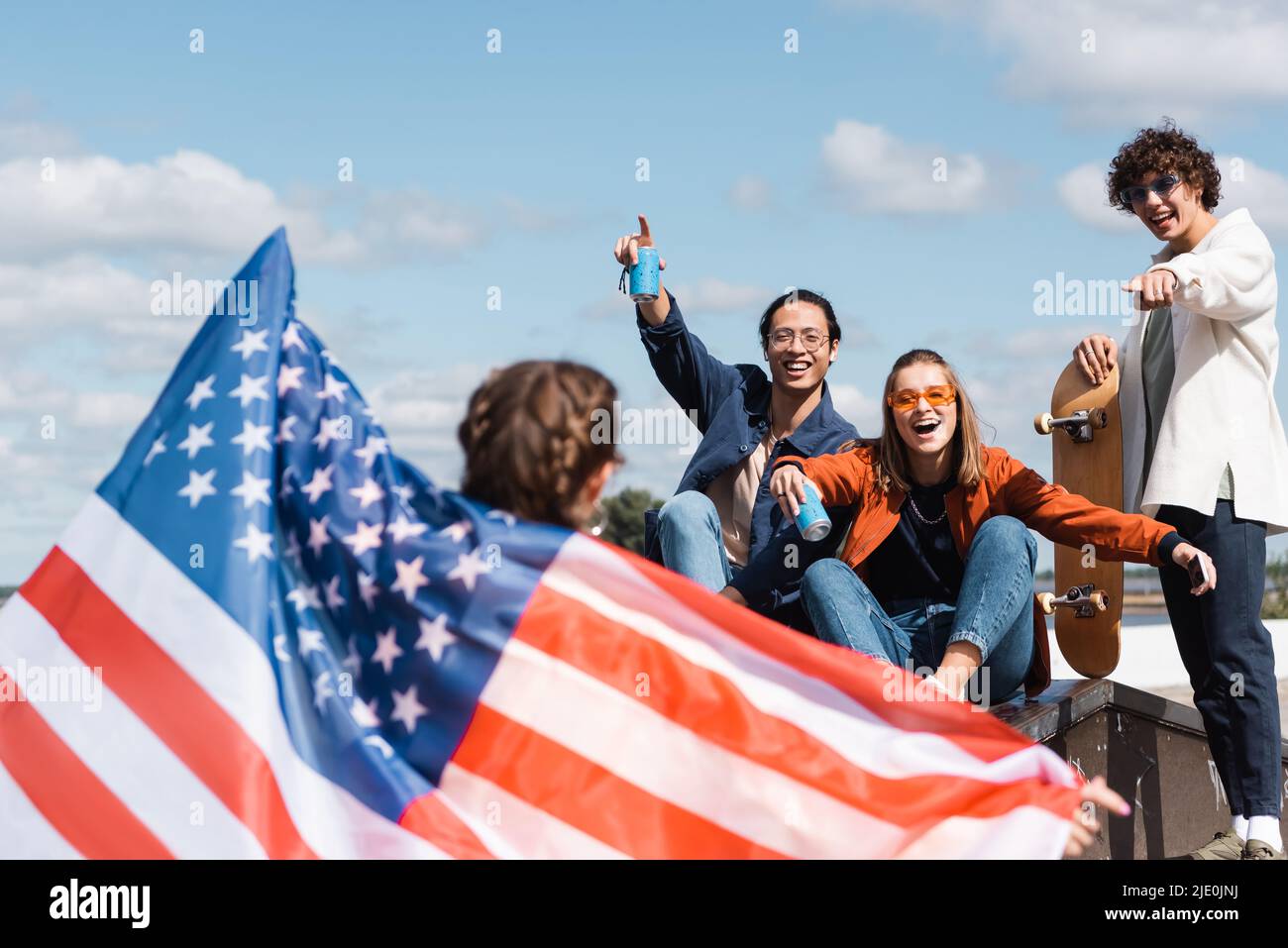 happy multiethnic friends pointing at blurred woman with usa flag ...