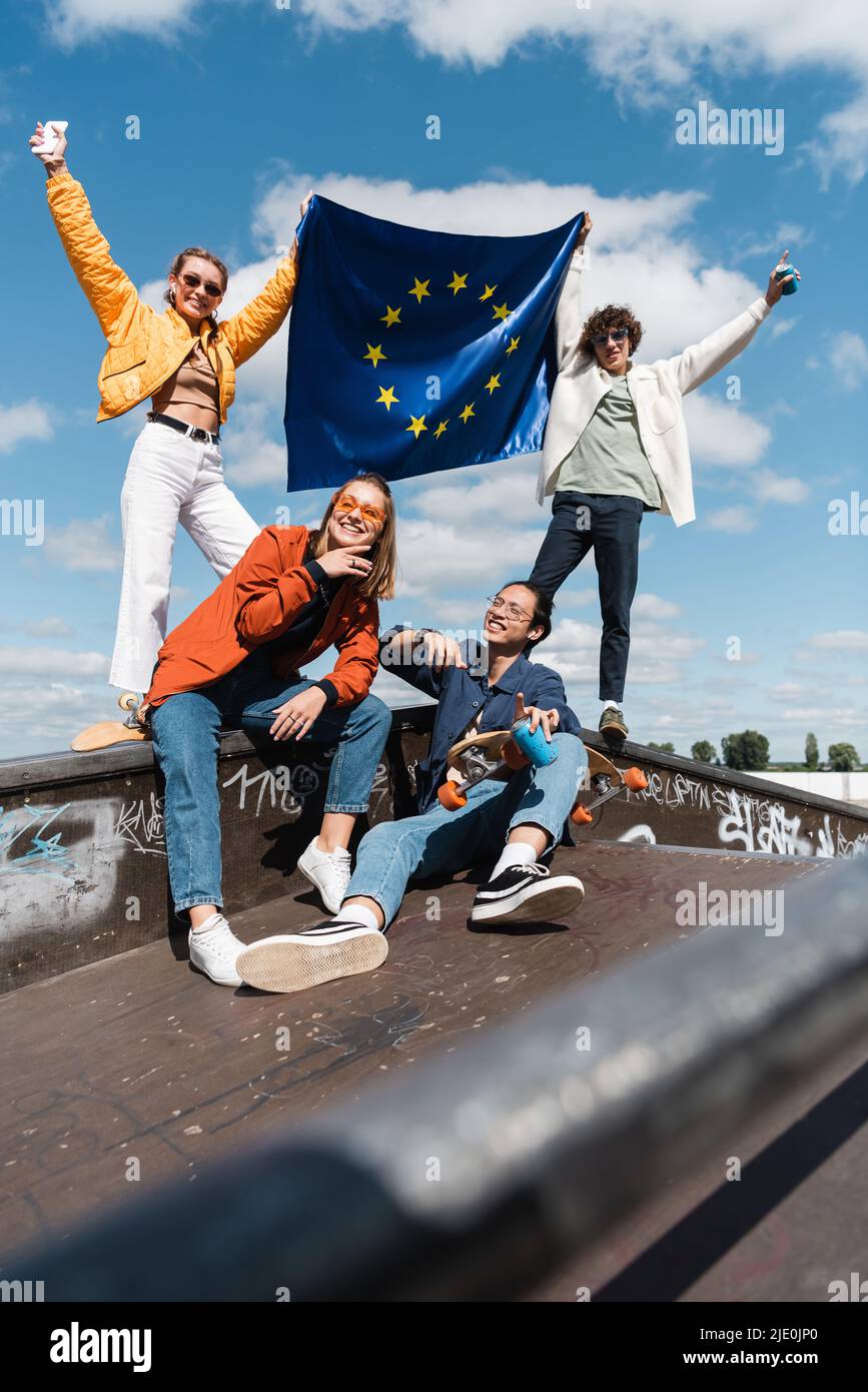 happy multicultural friends with european union flag in skate park ...
