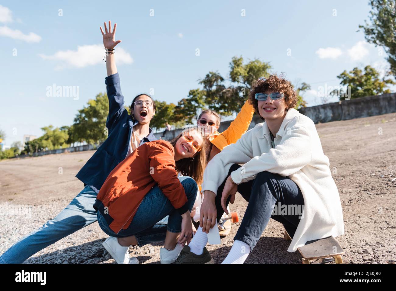 excited asian woman with raised hand screaming near smiling friends ...