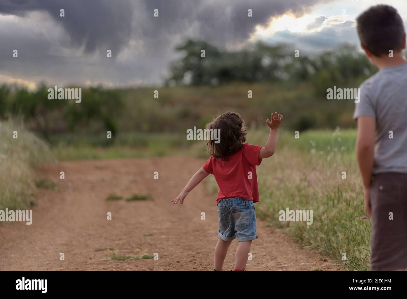 Two Caucasian boys walk through the field looking at a storm in the sky ...