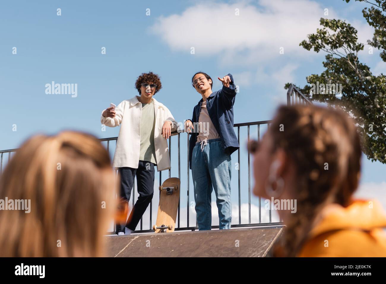 asian skater standing on skate ramp and pointing with finger at blurred ...