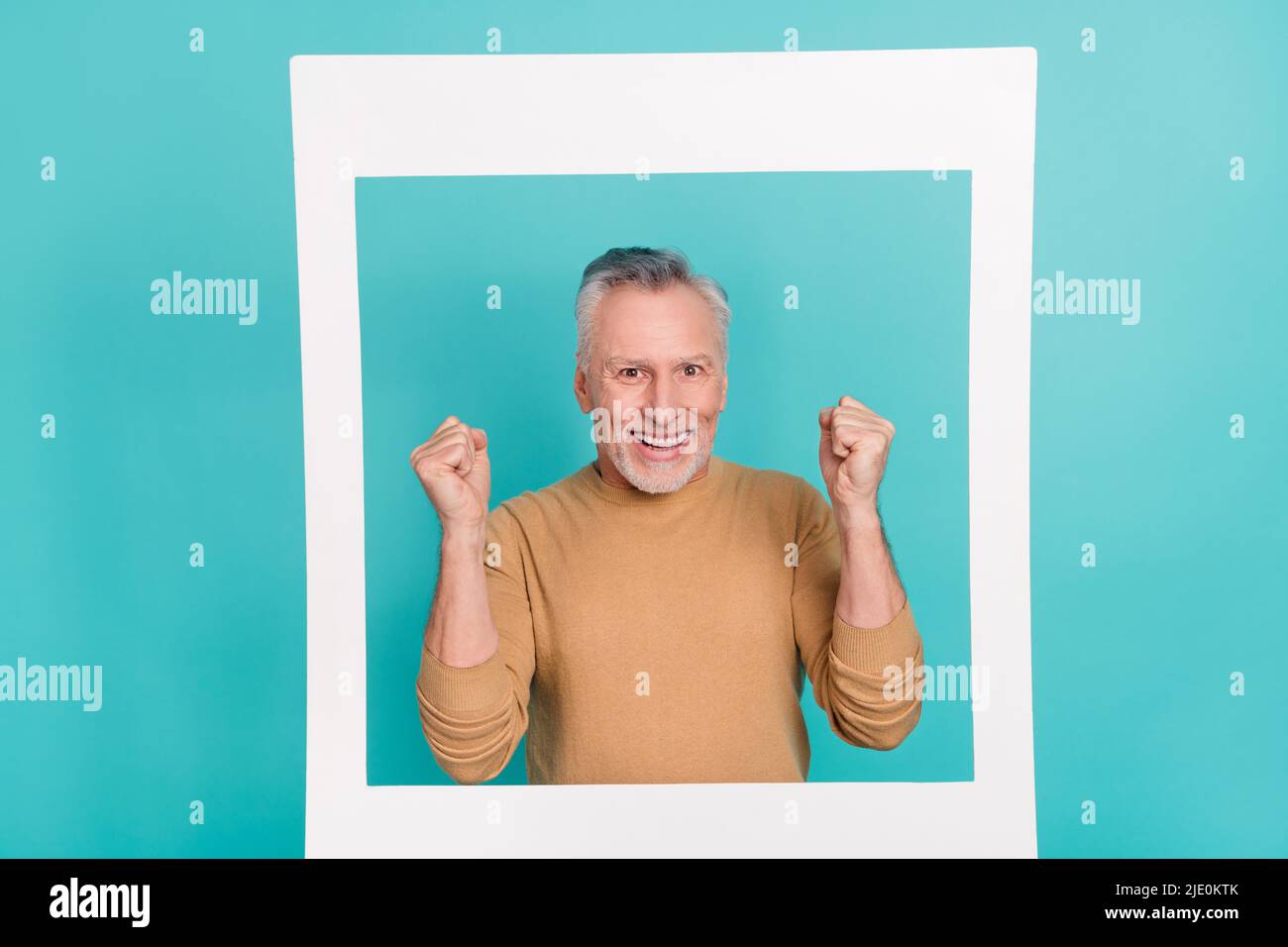 Portrait of delighted positive man raise fists success paper album card ...