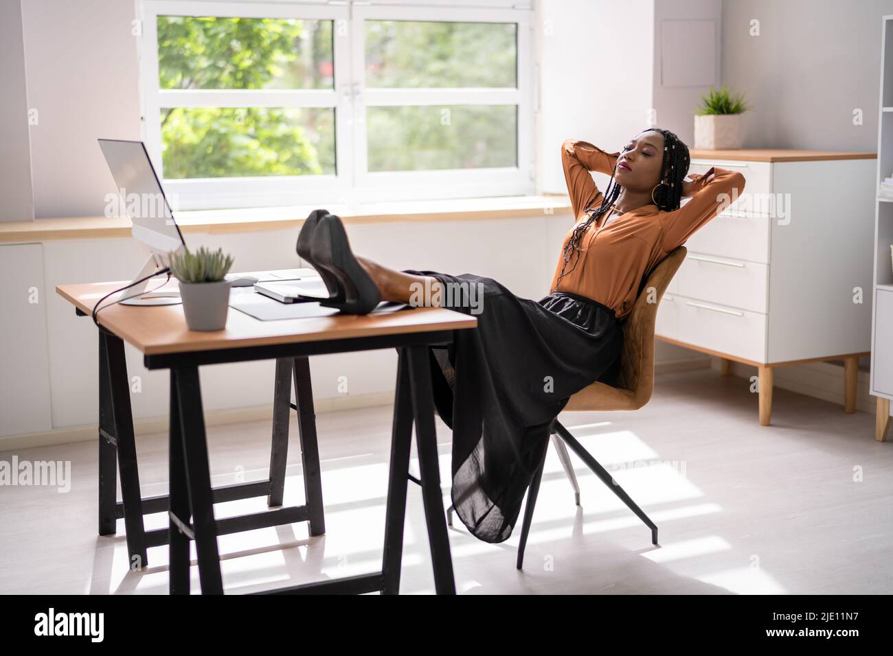 Side view of relaxed young businesswoman sitting feet up at office desk ...