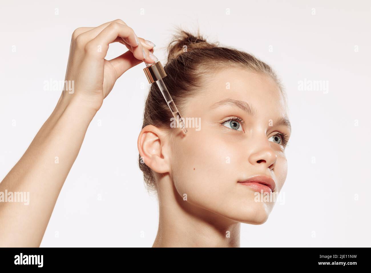 Close up beautiful young woman applying serum, oil on face on white ...