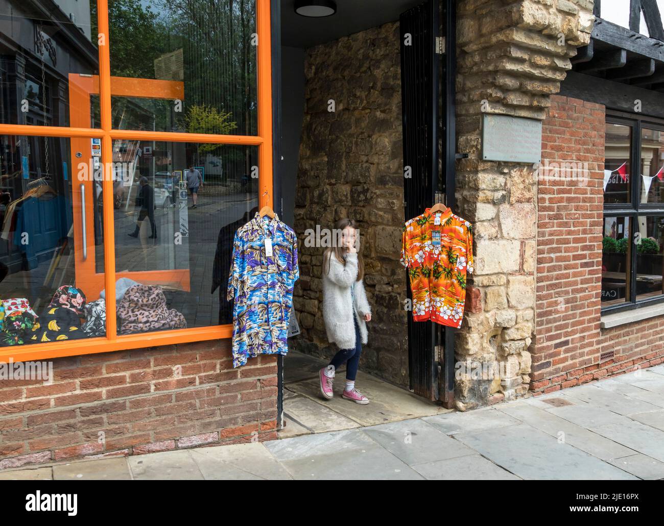 young girl running out of clothing store between two shirts hung in ...