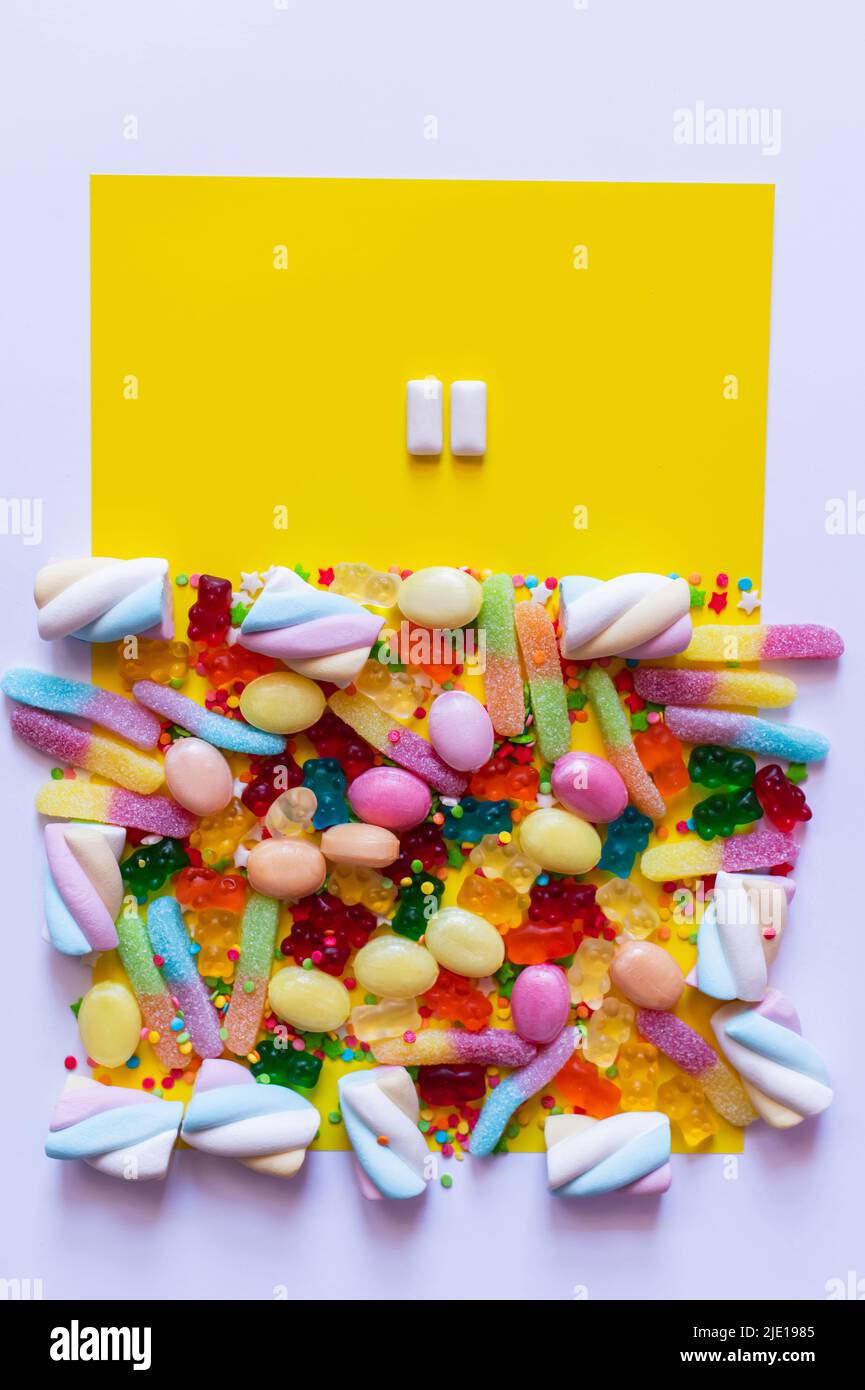 Top view of chewing gums near colorful sweets on white and yellow ...