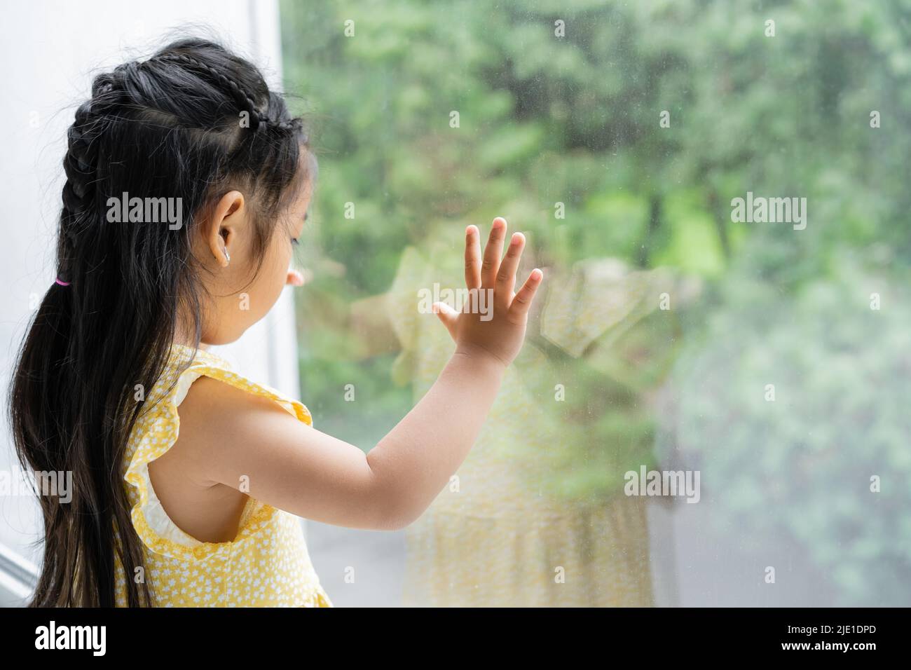 brunette and preschooler asian girl in yellow dress looking through ...