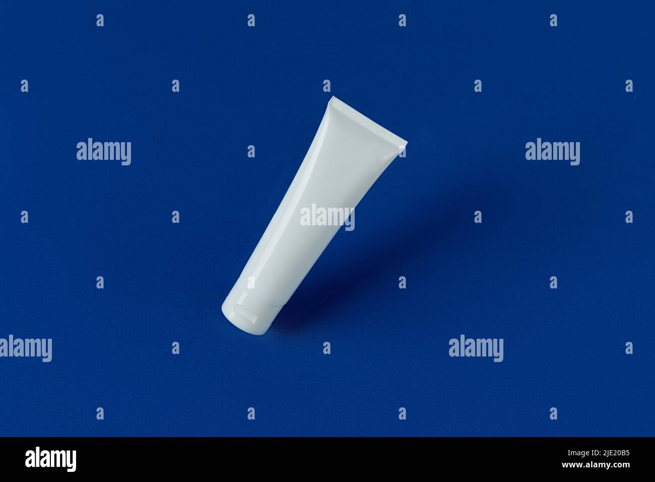 Top view blank white tube bottle with lotion cream or cleanser on blue ...