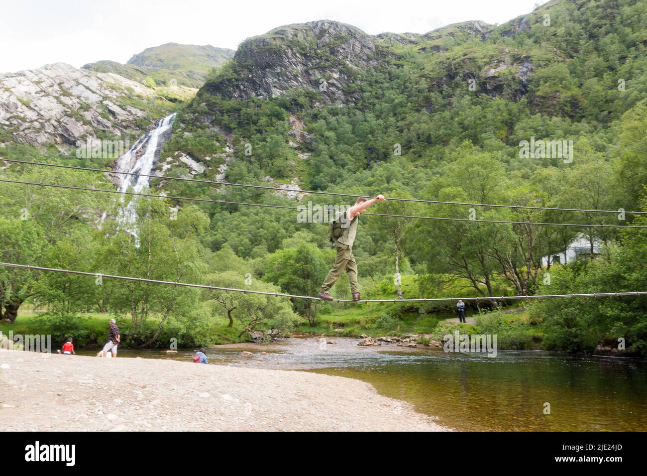 Man walking across Steall wire bridge over Water of Nevis river with ...