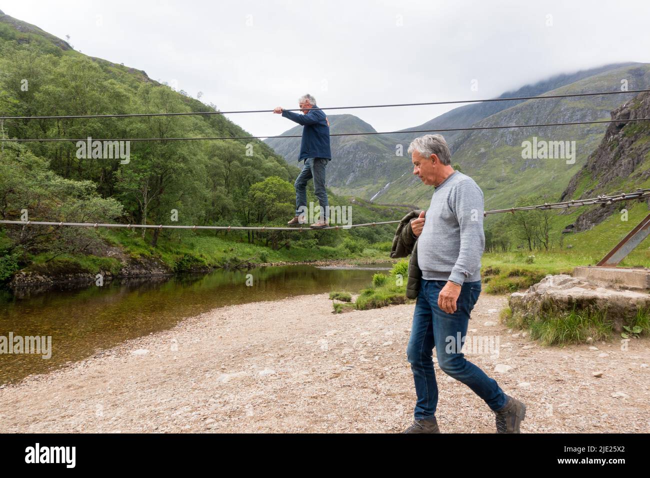 Man walking across Steall wire bridge over Water of Nevis river with ...