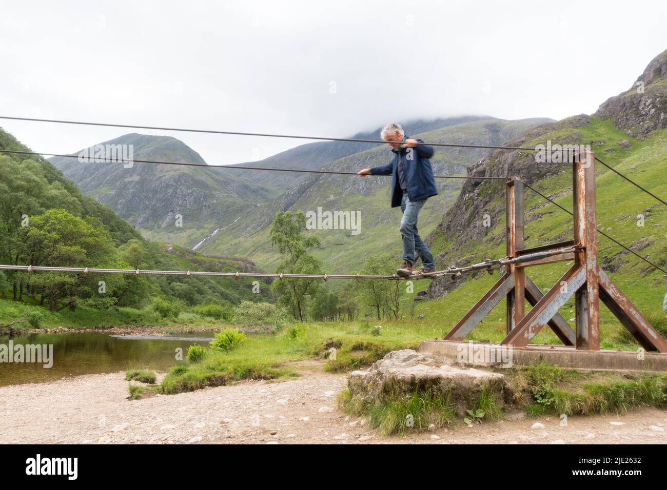 Man walking across Steall wire bridge over Water of Nevis river with ...