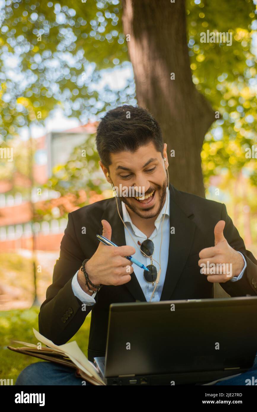 Hardworking urban student in the park talking on a video call with his ...
