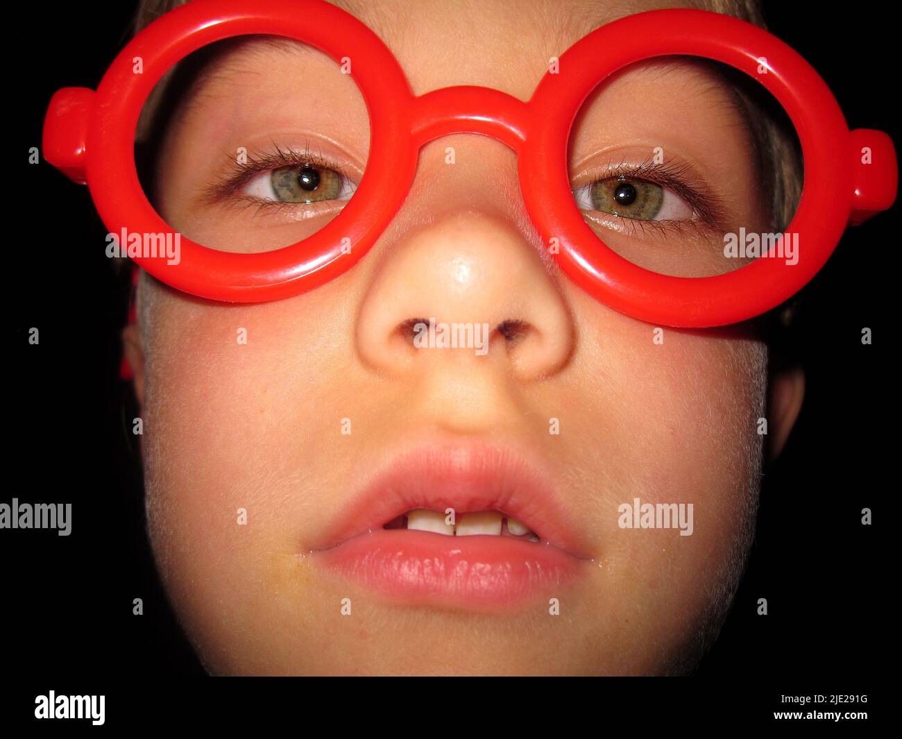 The boy's face in round red toy glasses is a close-up. portrait of a ...