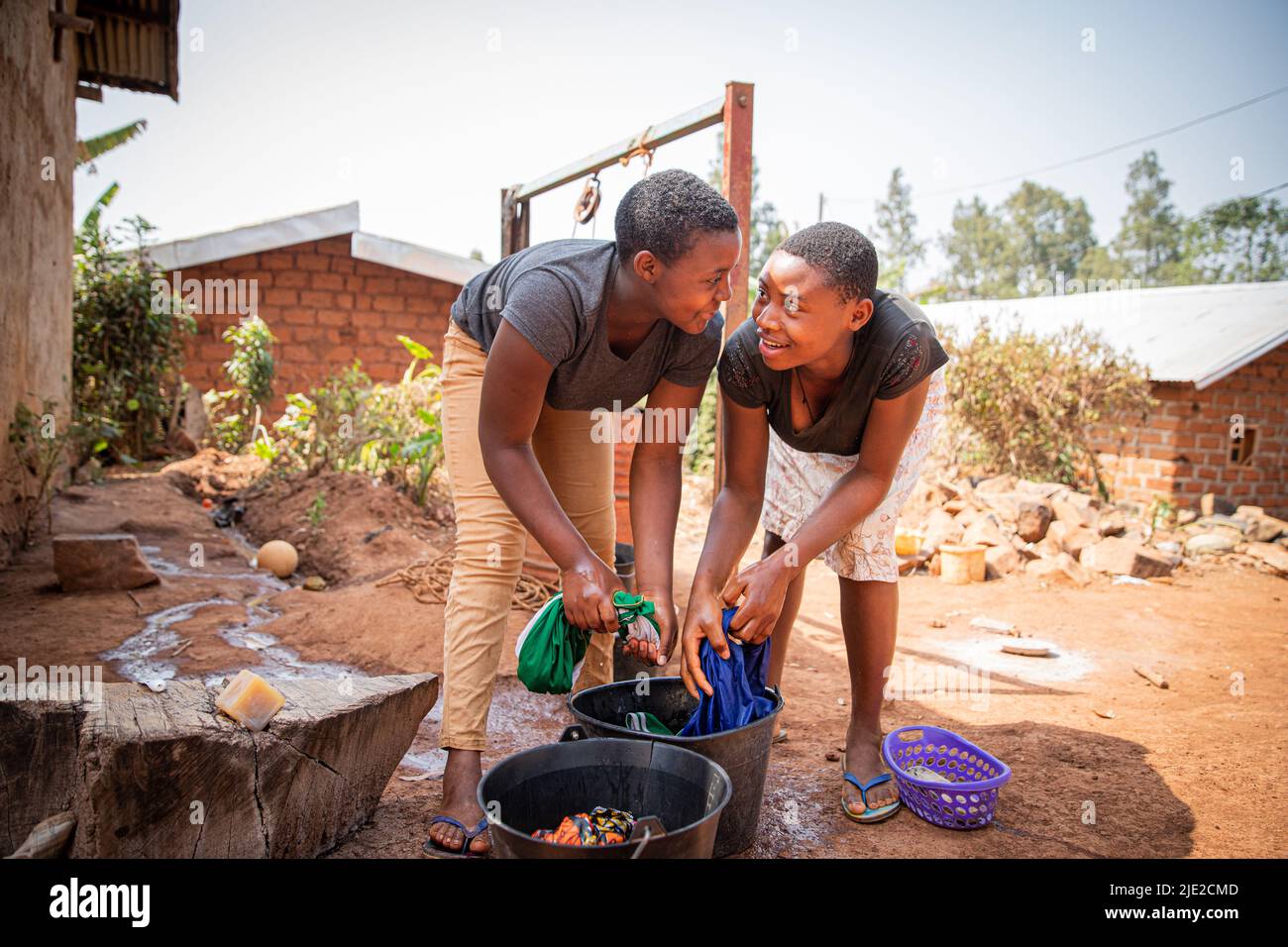 Two african girls wash clothes by hand using soap and a bucket ...