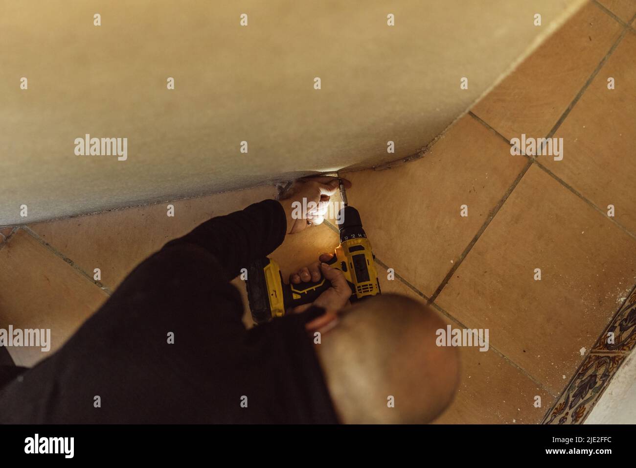 worker on his knees unscrewing with an electric screwdriver the screws ...