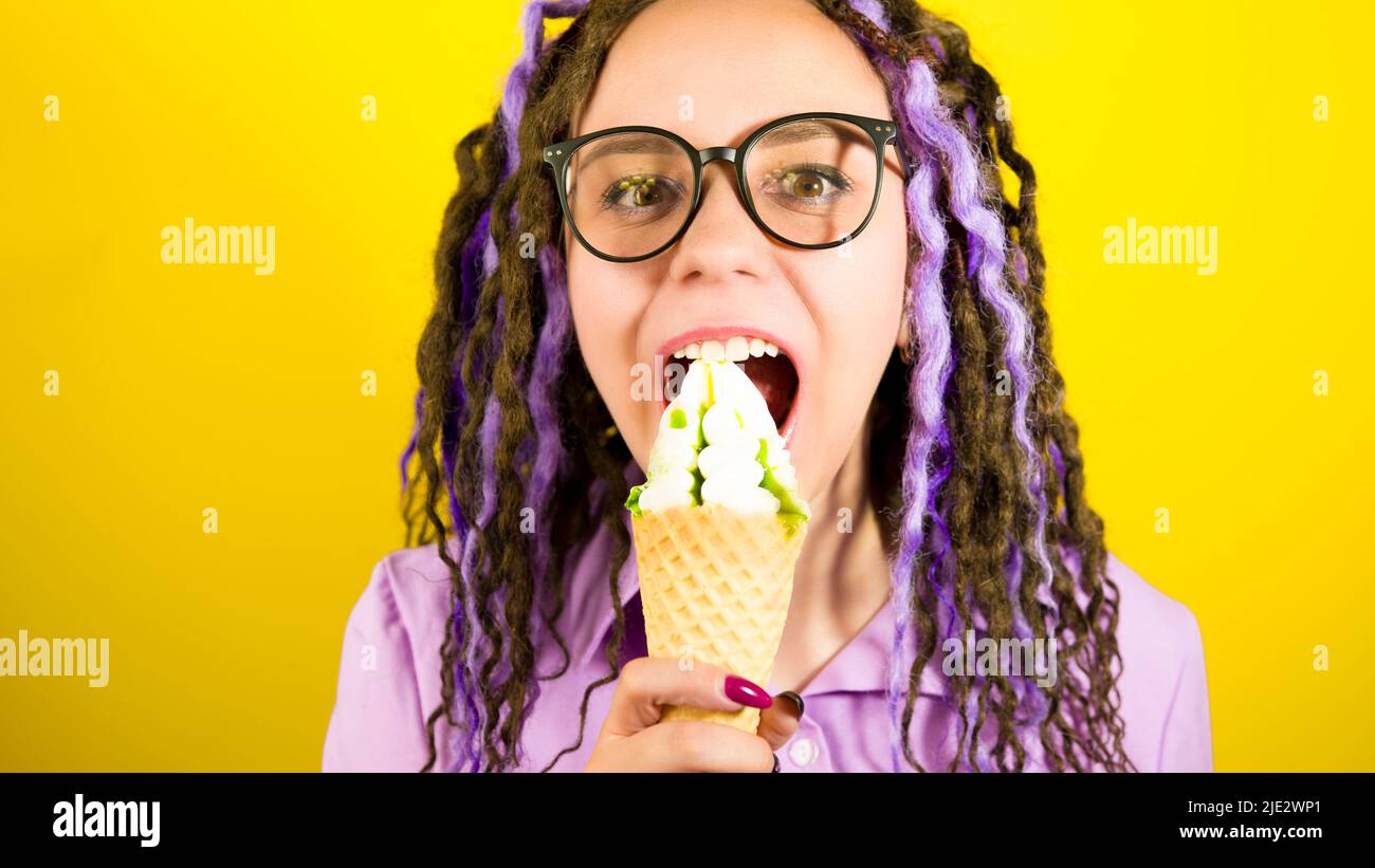 Young beautiful woman in glasses biting ice cream, looking at camera ...