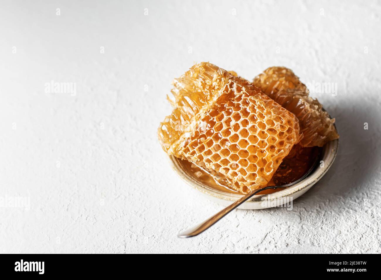 Honey in honeycomb in a saucer with spoon on a white background. Copy ...