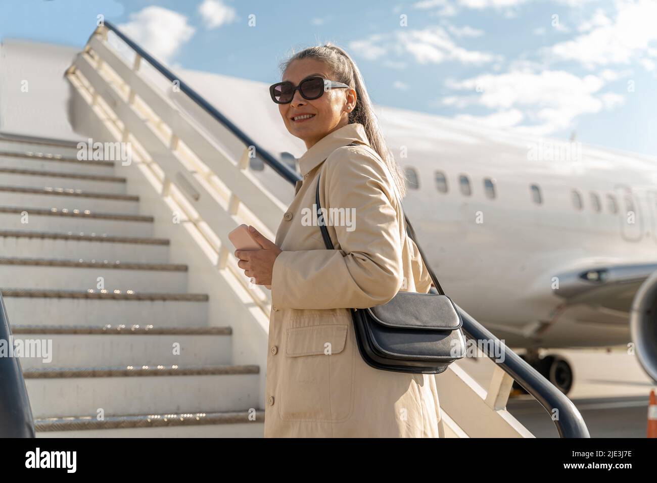 Happy woman passenger in sunglasses standing on aircraft stairs before boarding at airport Stock ...