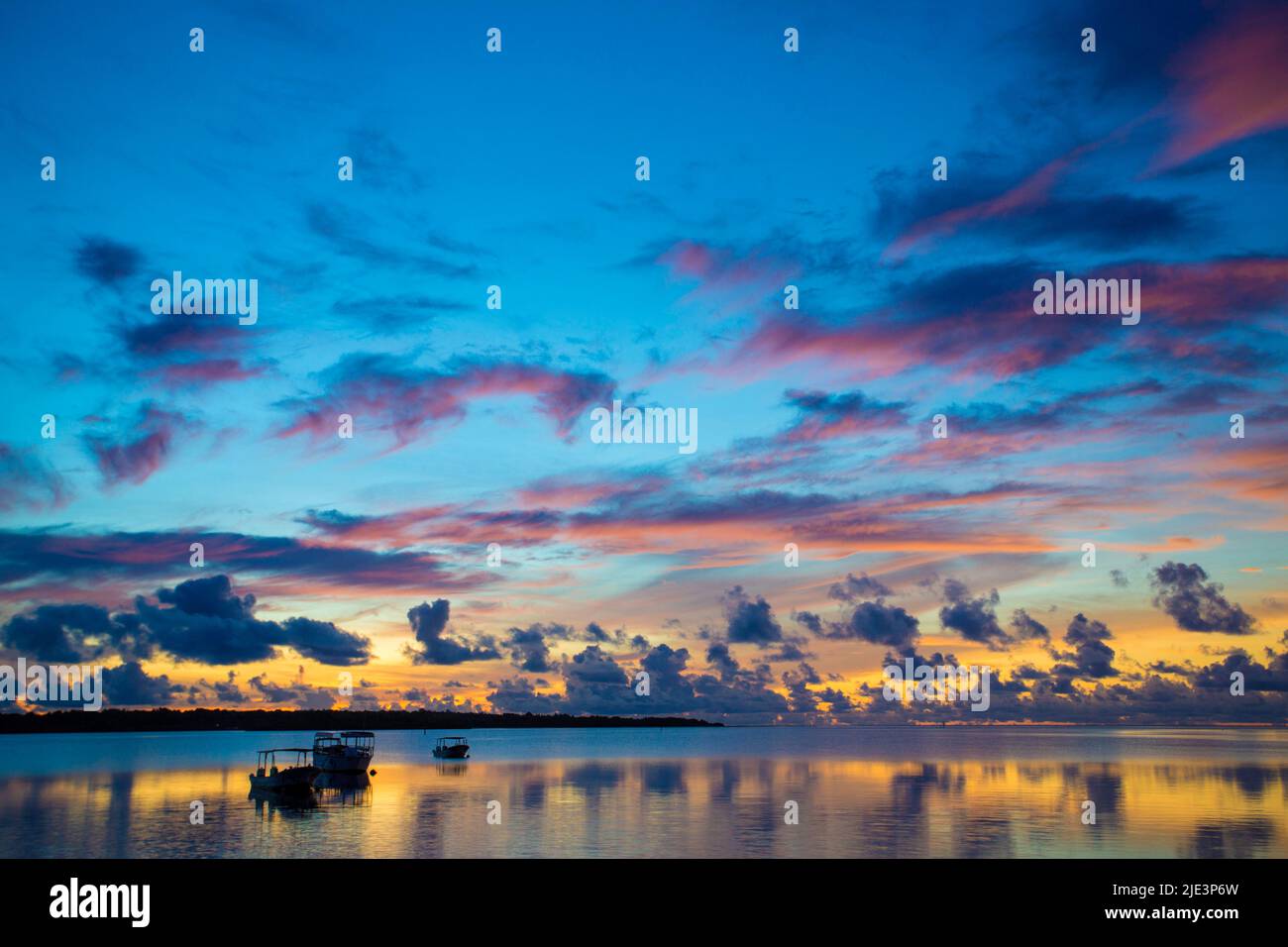 The sky lights up at dawn with boats floating on still waters off the ...