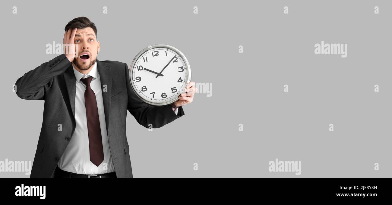 Stressed businessman holding clock on grey background with space for ...