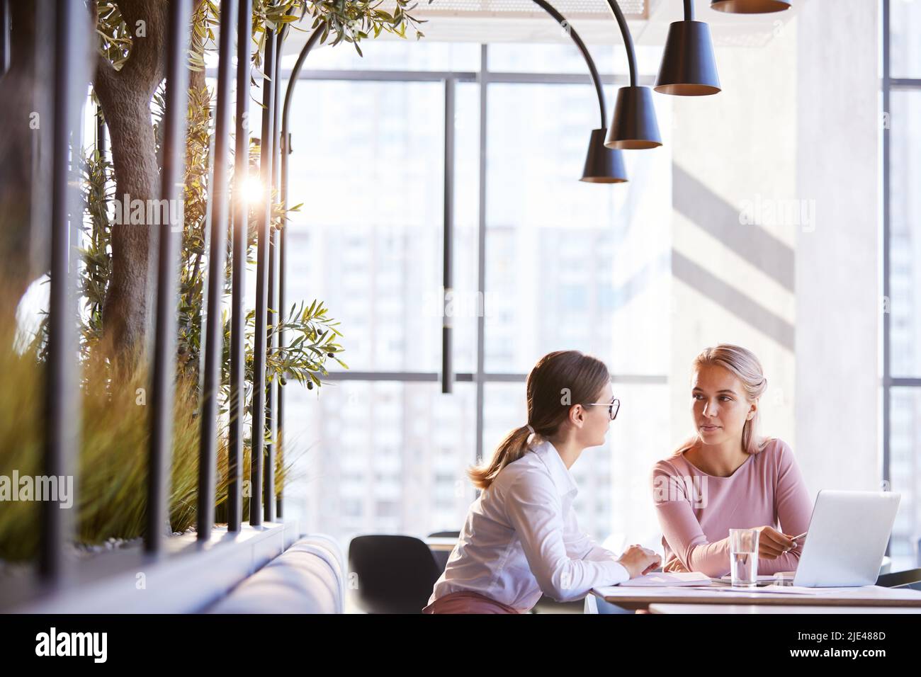 Busy young women in strict clothes sitting at table in cozy restaurant ...