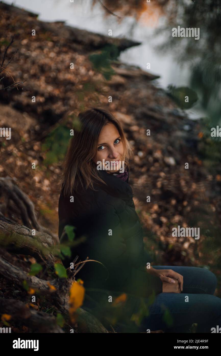 Blissful blonde woman sitting on tree roots in forest, smiling, looking ...