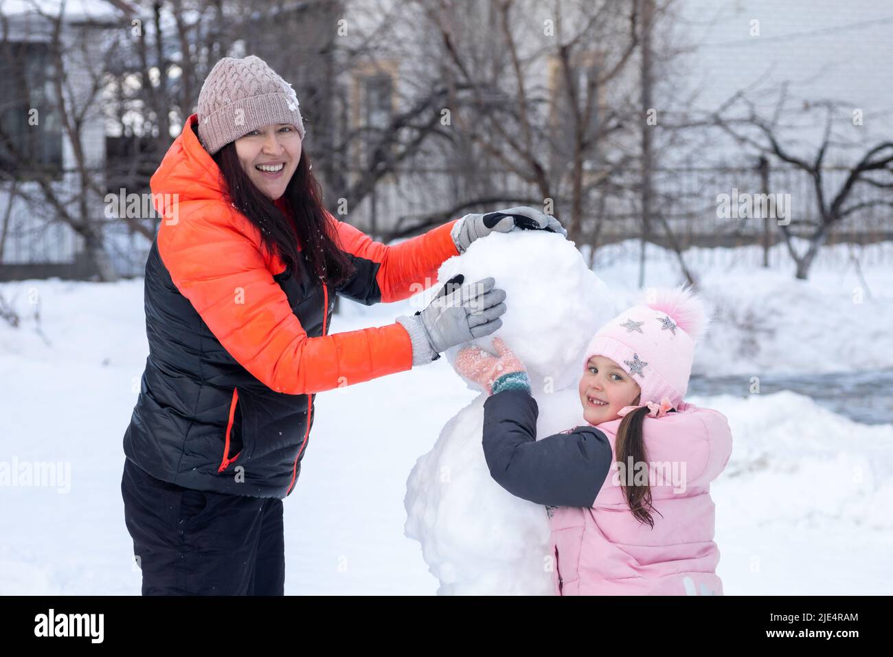 Little girl and mother putting middle part of snowman on bottom part ...