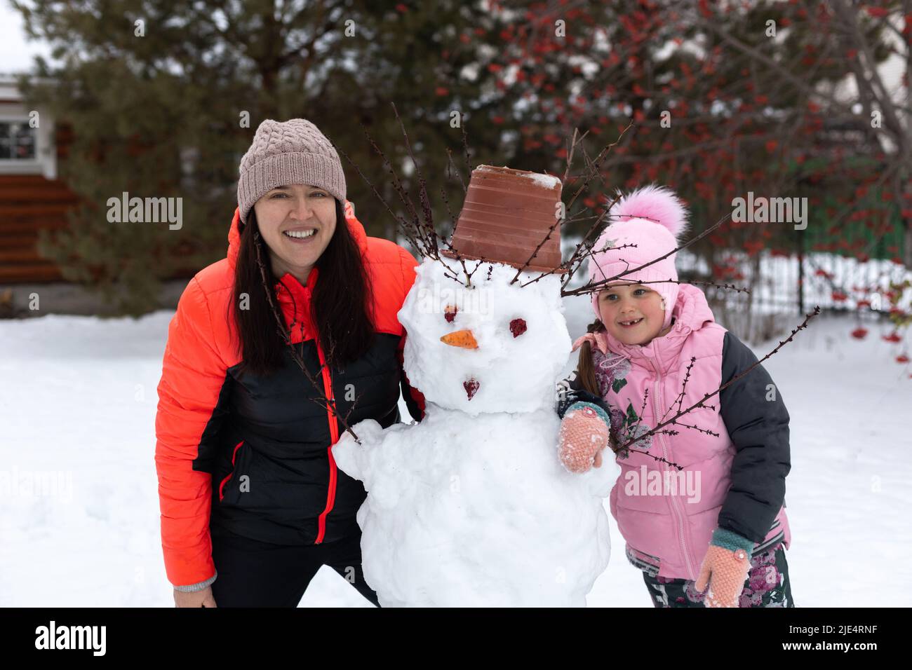 Smiling young girl and middle aged woman hugging snowman in daytime ...