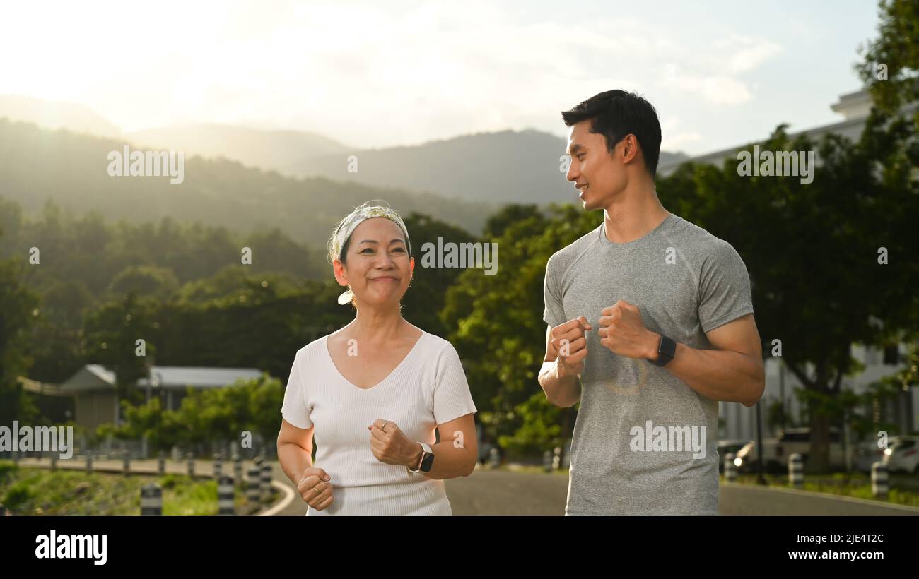 Happy middle aged woman jogging at the park with her personal trainer ...