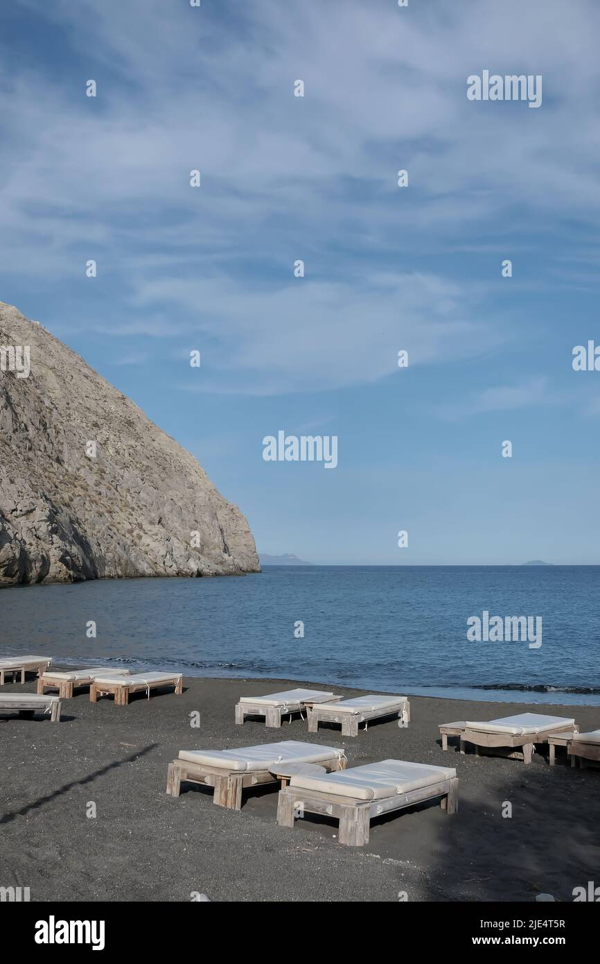 Sun beds and a sun umbrella at the famous black sandy beach of Perissa ...