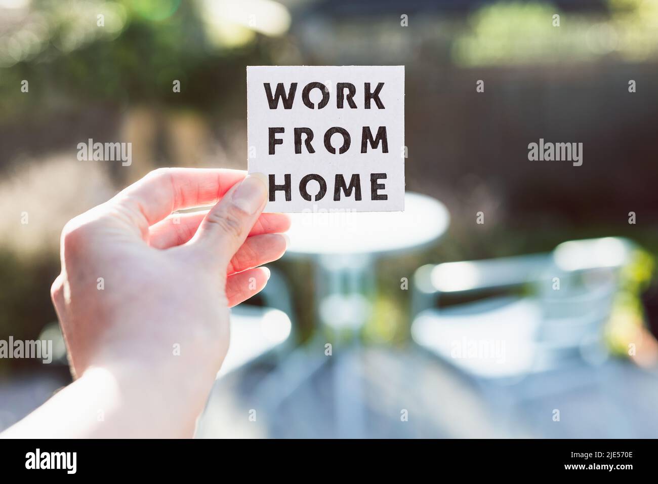 work from home sign being hold in front of sunny out of focus backard ...