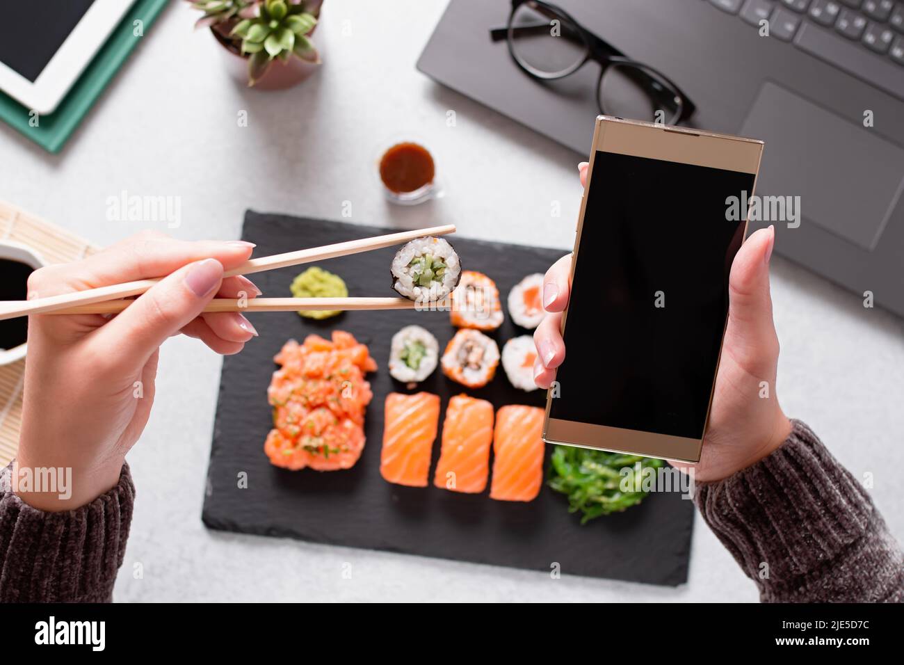 Woman eating sushi takeaway at work desk overhead. Eating sushi for ...