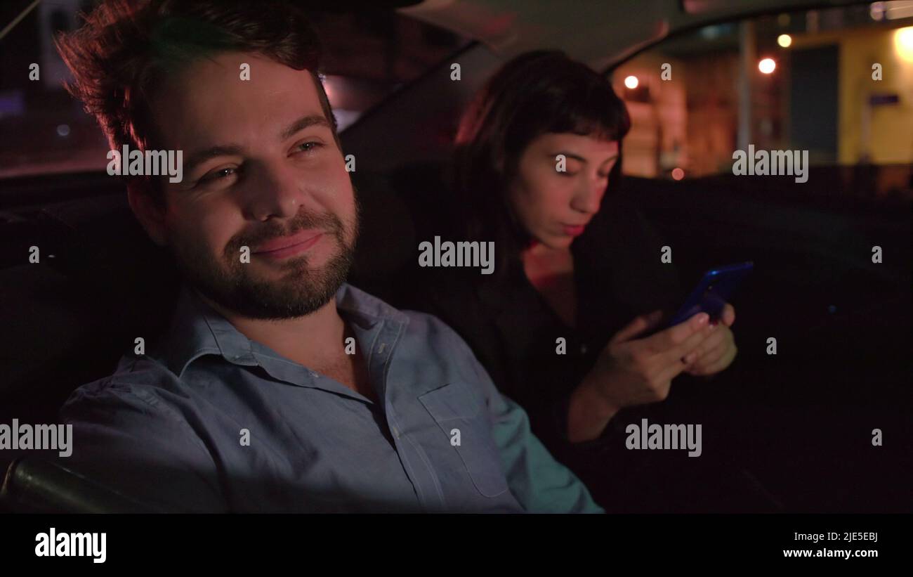 Happy man commuting from work in taxi car backseat at night looking out ...