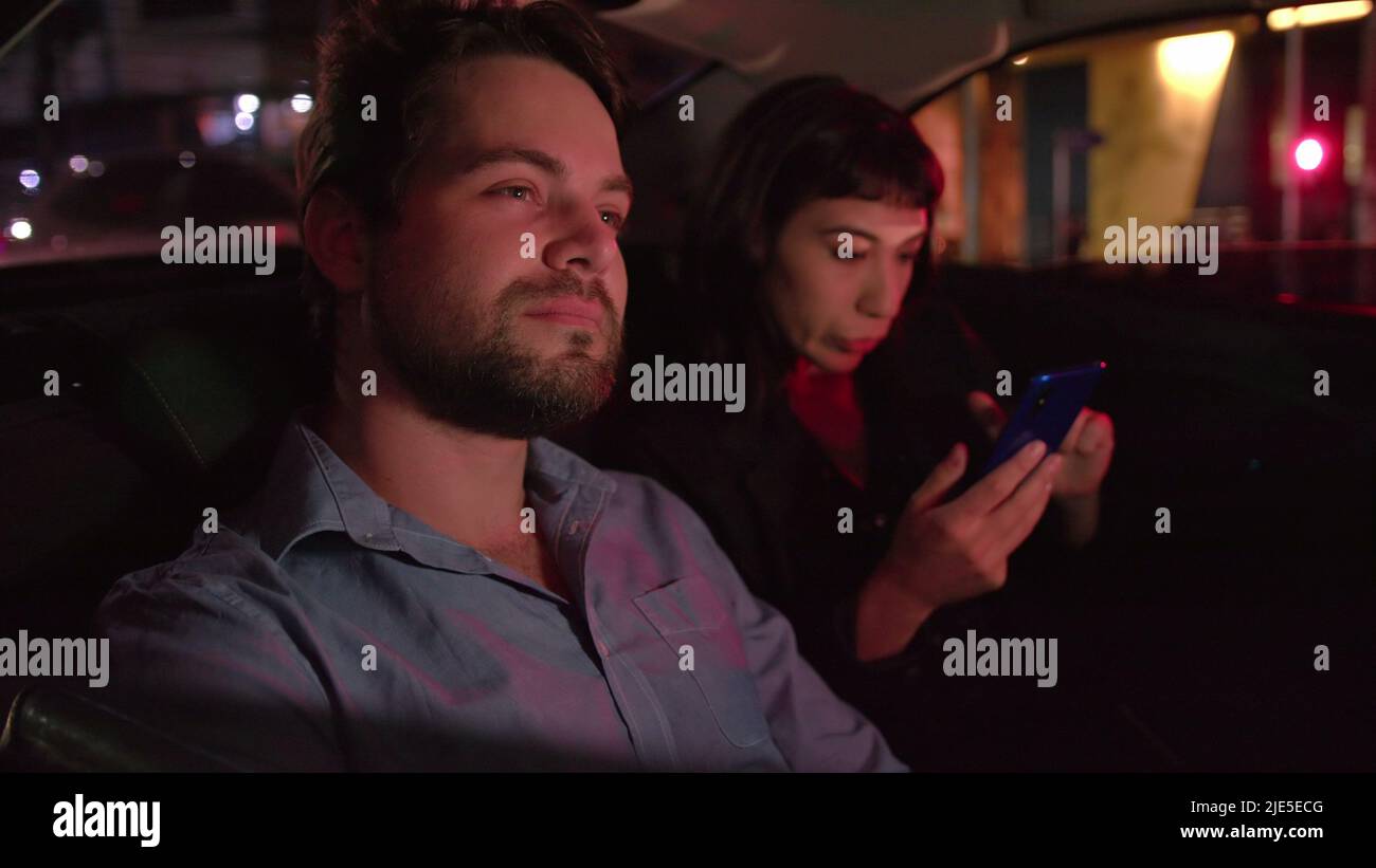 Happy man commuting from work in taxi car backseat at night looking out ...