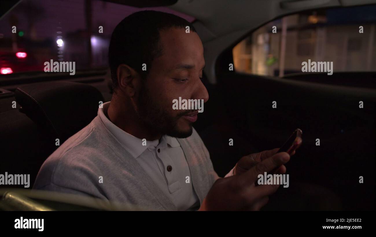 Passenger in the backseat of a car looking at cellphone device at night ...