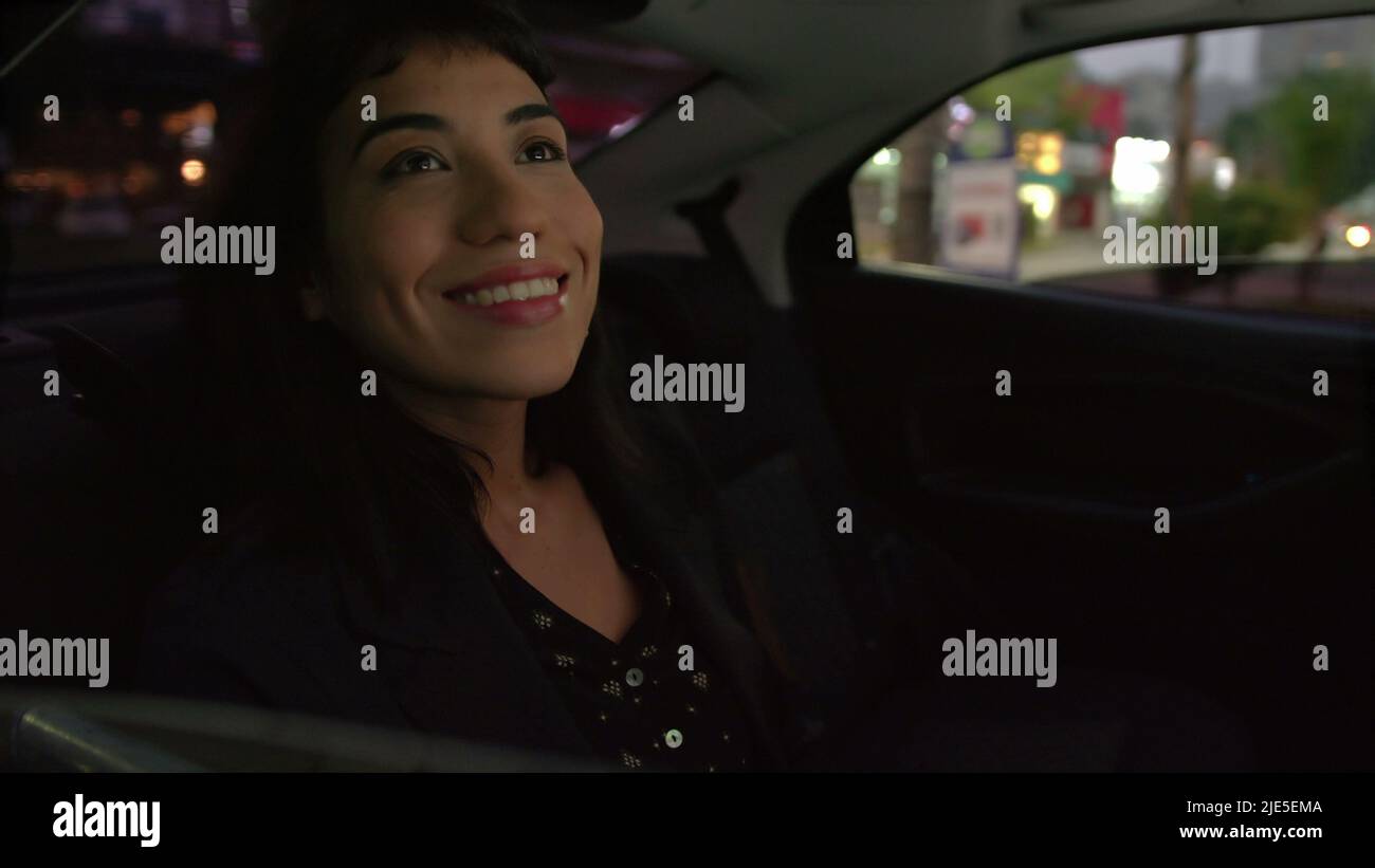 One happy hispanic woman sitting in car backseat looking out window ...