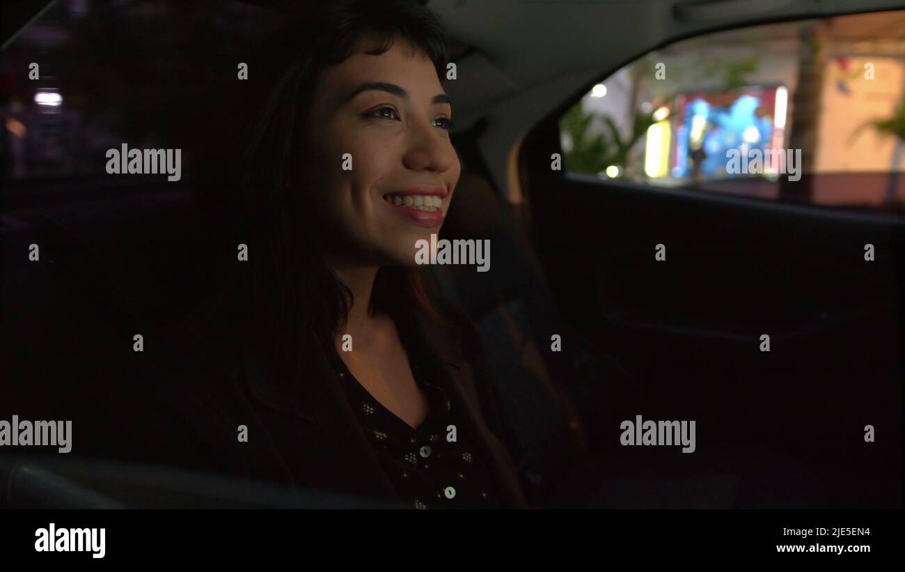 One happy hispanic woman sitting in car backseat looking out window ...