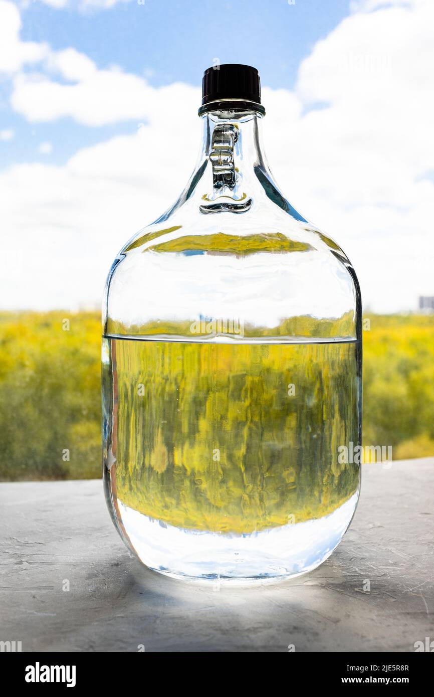 five-liter glass bottle with alcohol on concrete window sill over ...