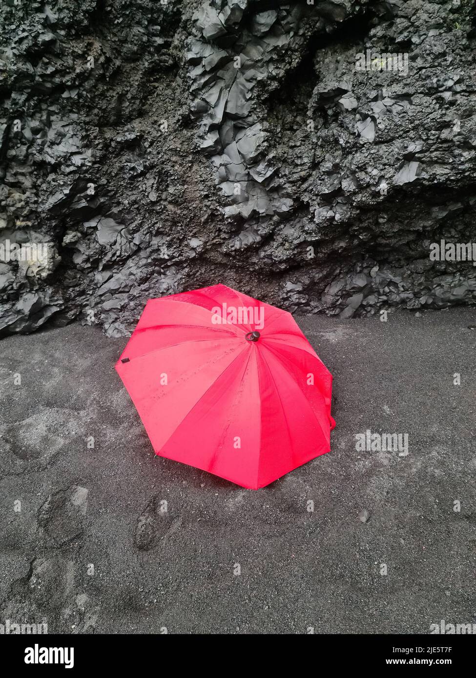 A lone red umbrella on the endless black beaches of Iceland in front of ...