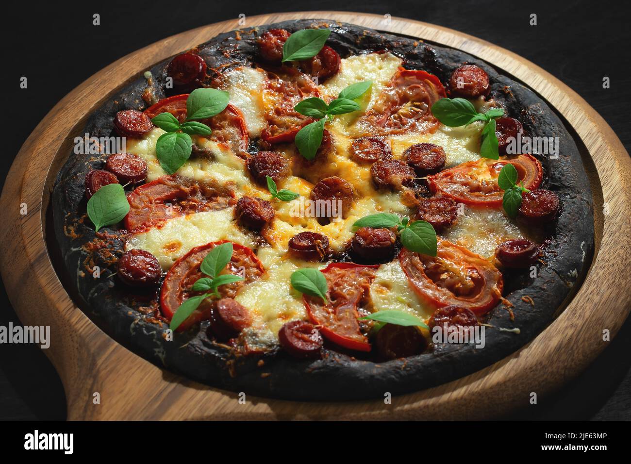 Black pizza with tomatoes, sausages, mozzarella and basil. Dough with ...
