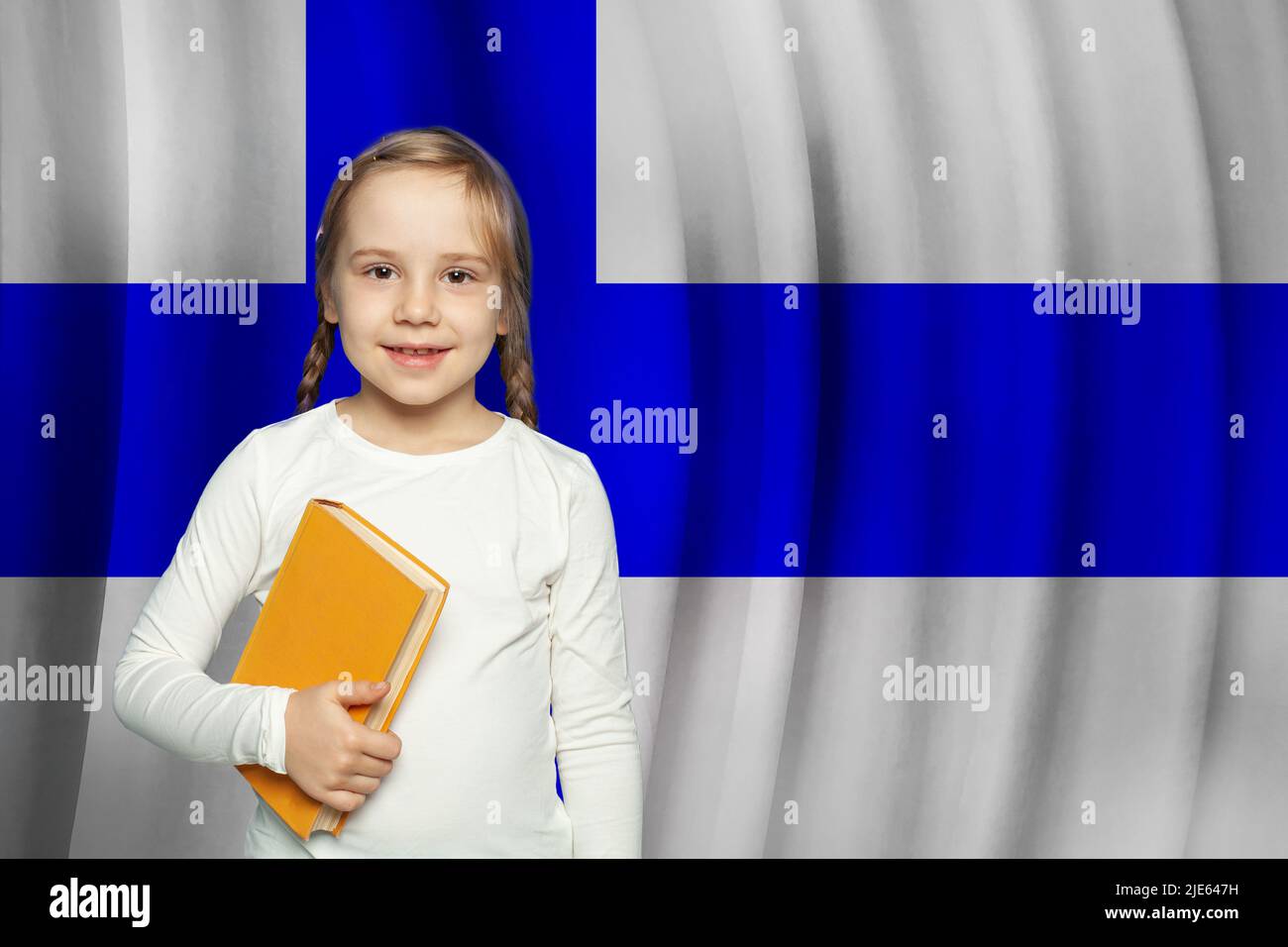 Beautiful smiling little kid with book standing against Finnish flag ...