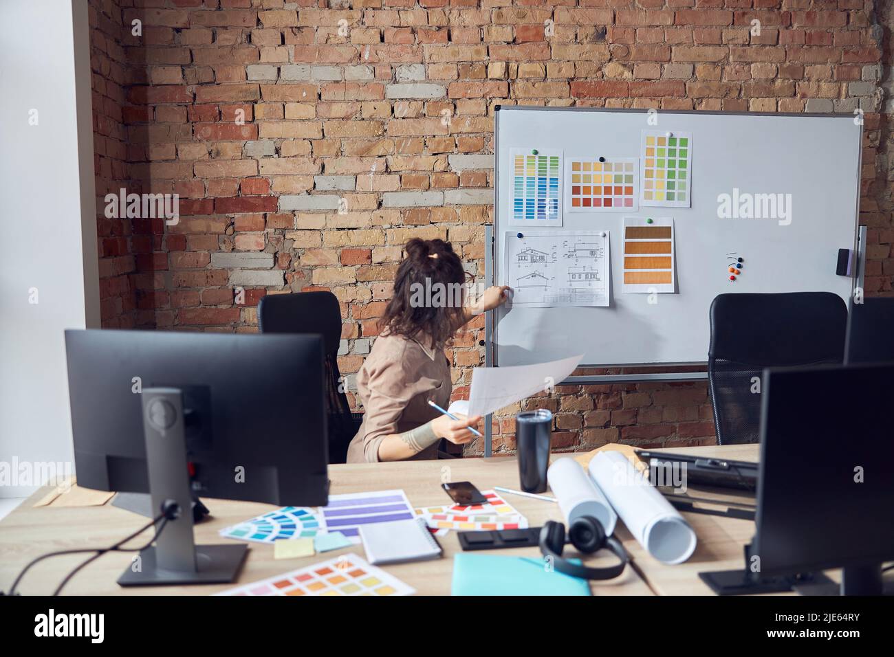Woman designer attaching blueprint paper and color samples on board ...