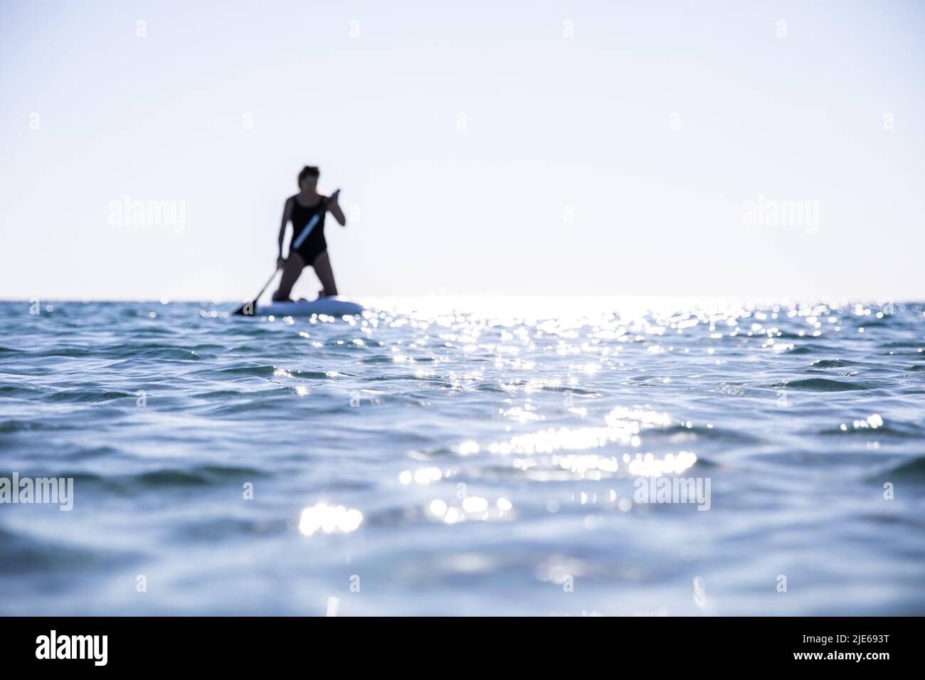 Silhouette of a woman on sap board with a paddle in her hands against a ...